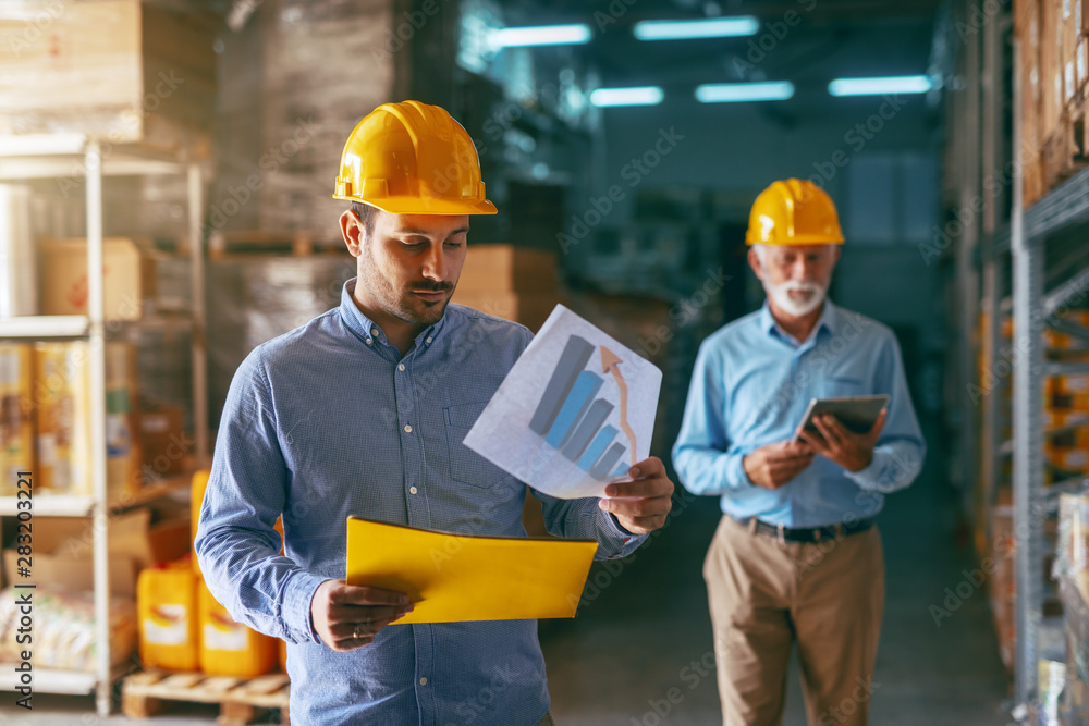 Supervisor holding folder with charts and analyzing sales while ...