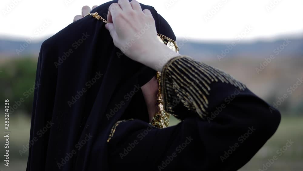 gorgeous arabian woman in black hijab puts on golden tribal face veil ...