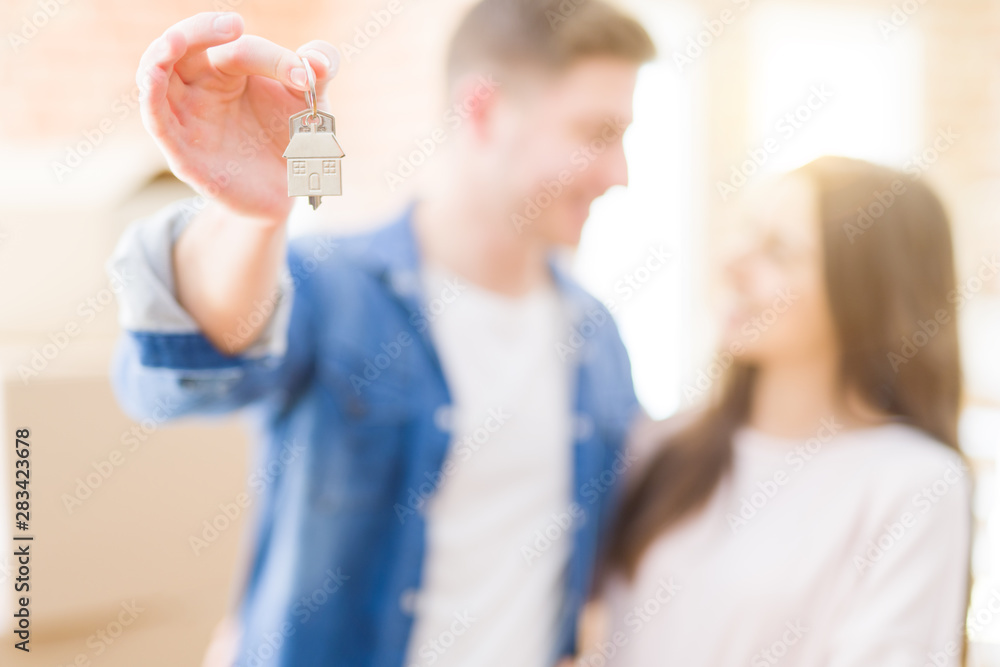 Beautiful young couple hugging in love and showing keys of new house ...