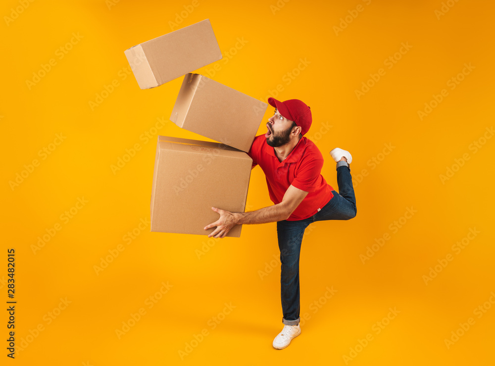 Full length portrait of shocked delivery man in red uniform carrying ...