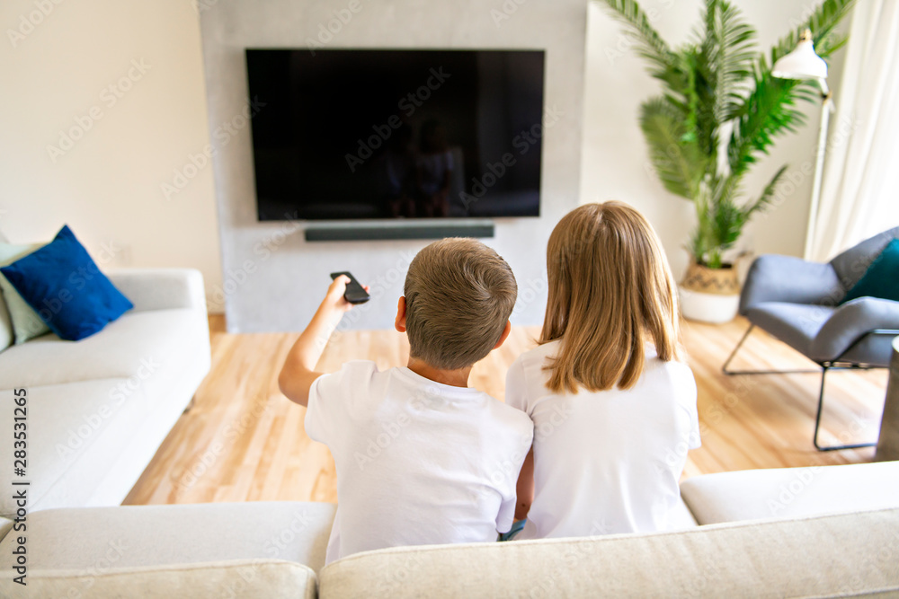 A two family brother and sister holding remote control and watching TV ...
