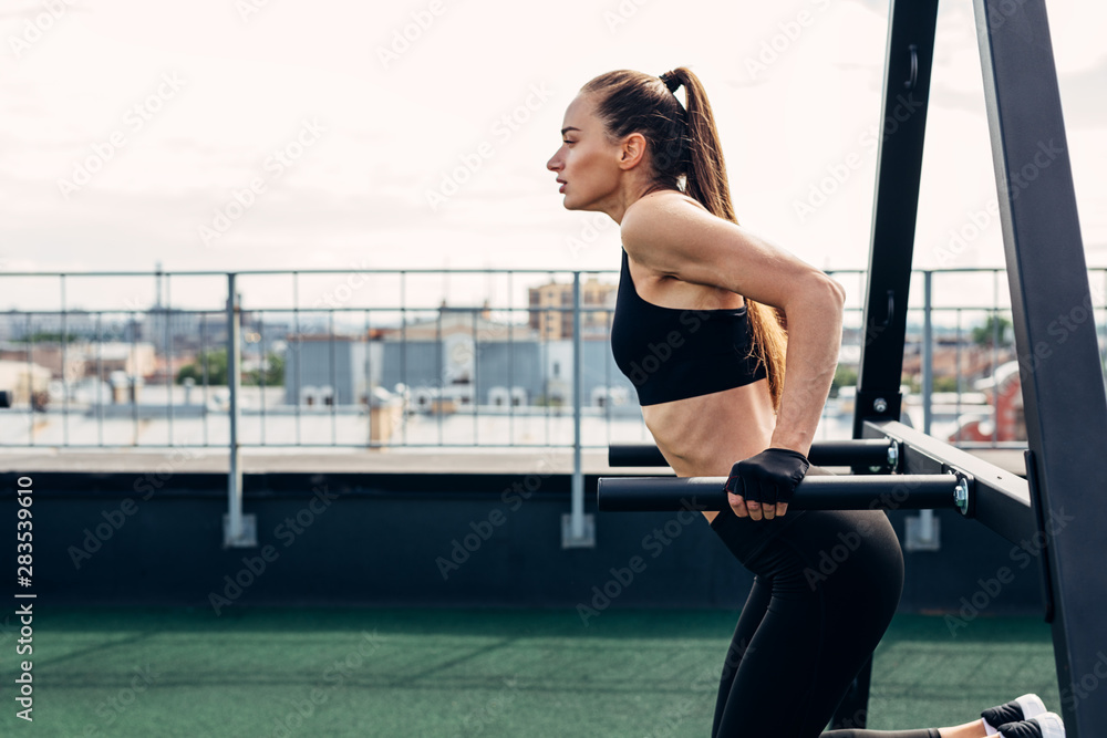 Side view of fitness woman doing triceps dip exercises on power rack ...