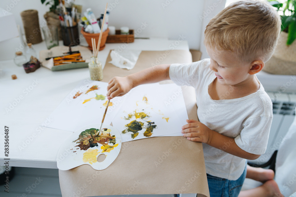 Cute first grade child boy is painting on paper sheet with brush at ...