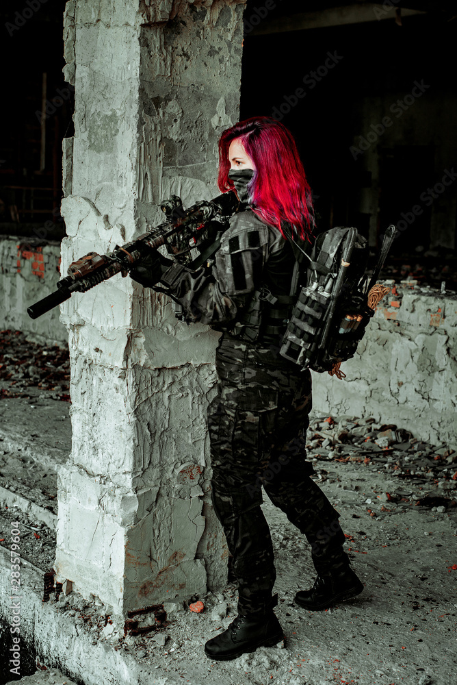 Red-hair airsoft woman in uniform with machine gun stand beside column ...