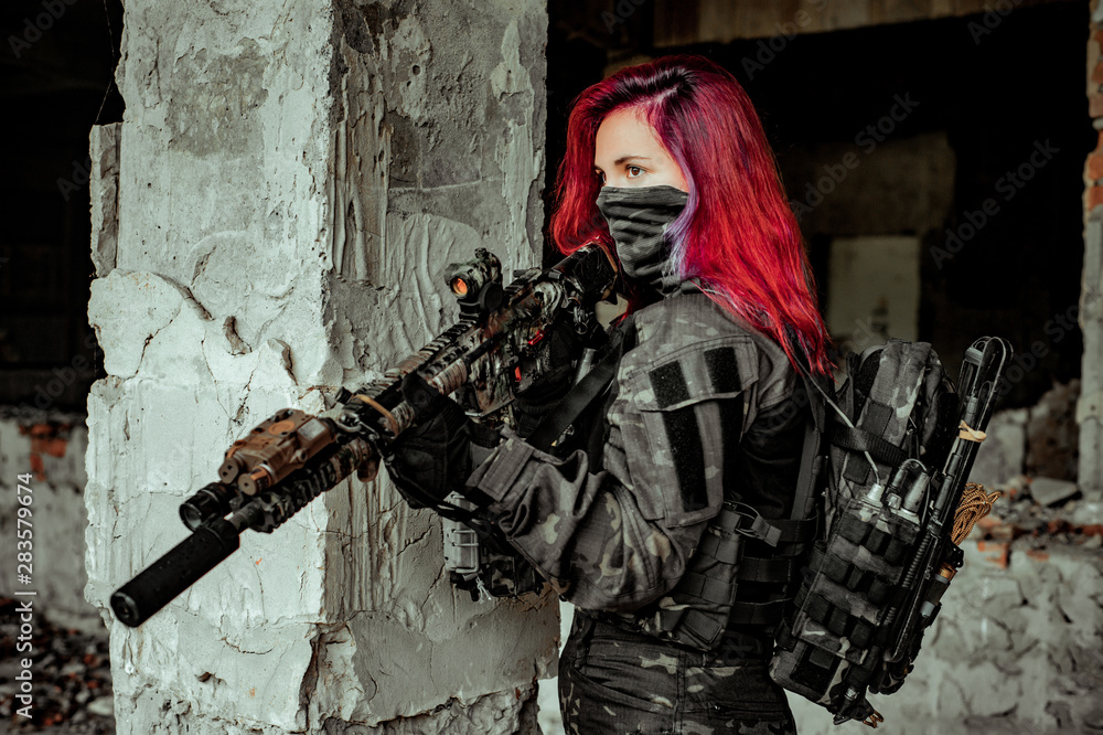 Red-hair airsoft woman in uniform with machine gun stand beside column ...