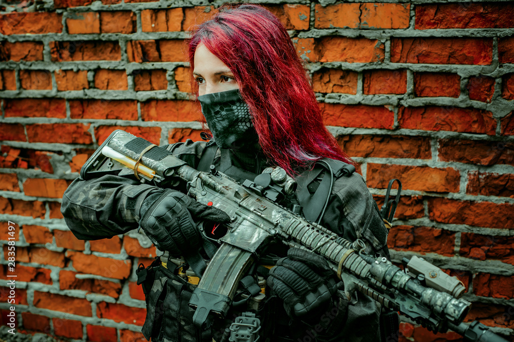 Airsoft red-hair woman in uniform with machine gun beside brick wall ...