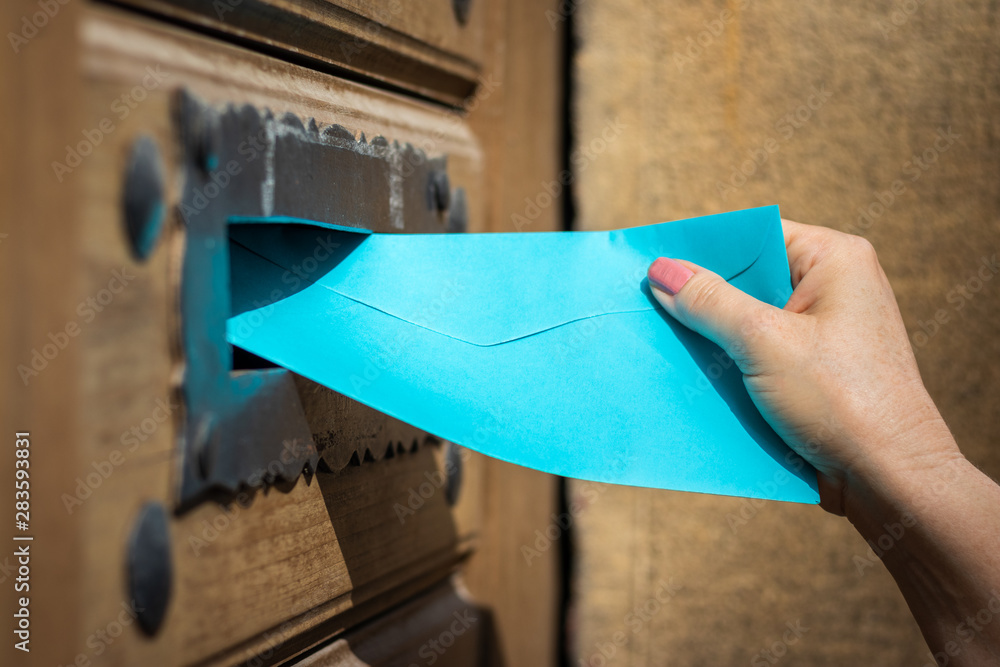 Woman inserting blue envelope into mail slot. Delivering letter by mail ...