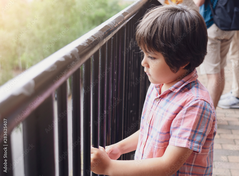 Lonely kid boy holding metal fence and looking down with sad face ...