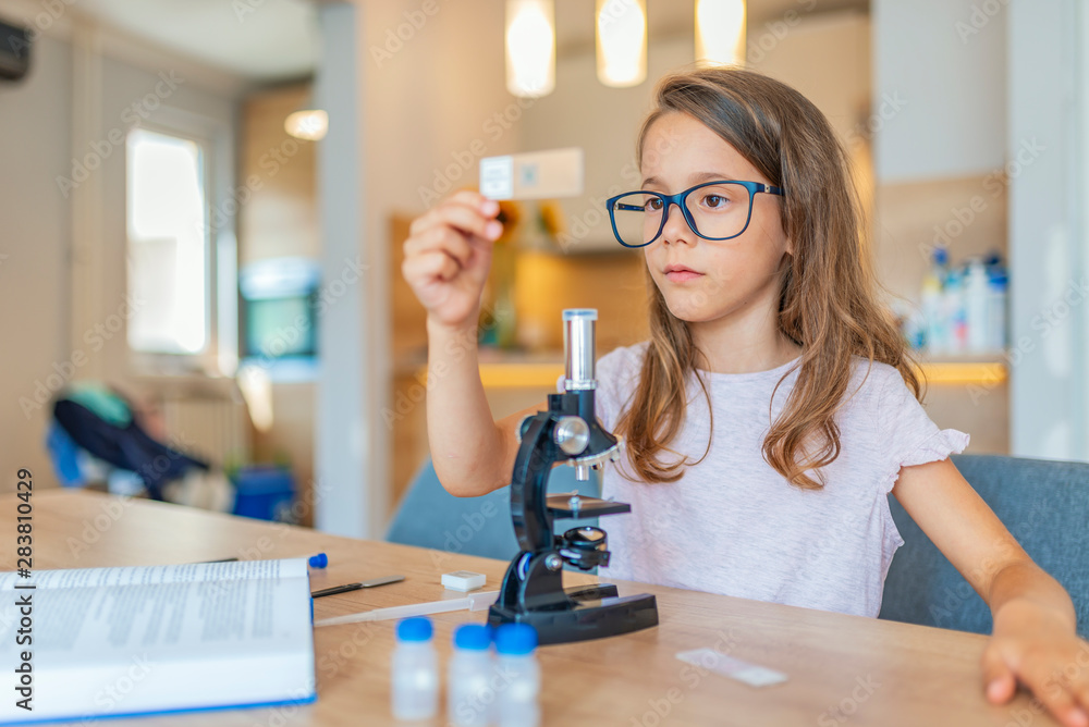 Preschool age girl looks into microscope. Child playing science in the ...