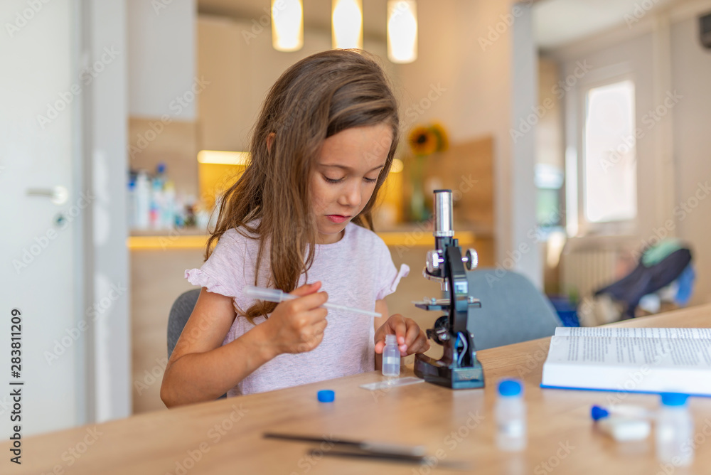 Foto de Confident little girl uses microscope at home. Beautiful ...