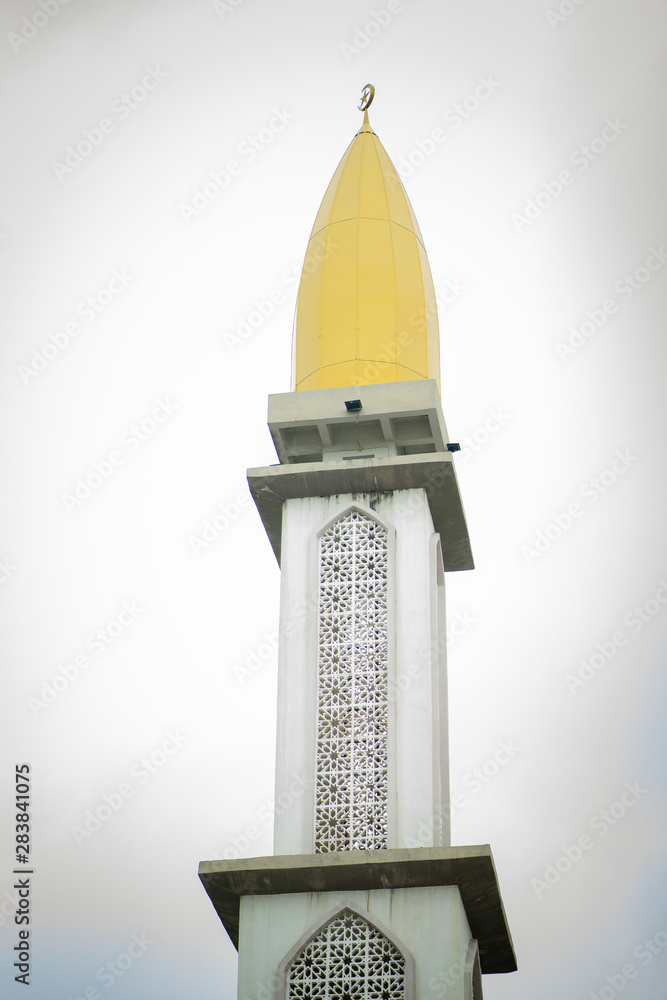 A tall white and yellow minaret of a Muslim mosque against the sky. One ...