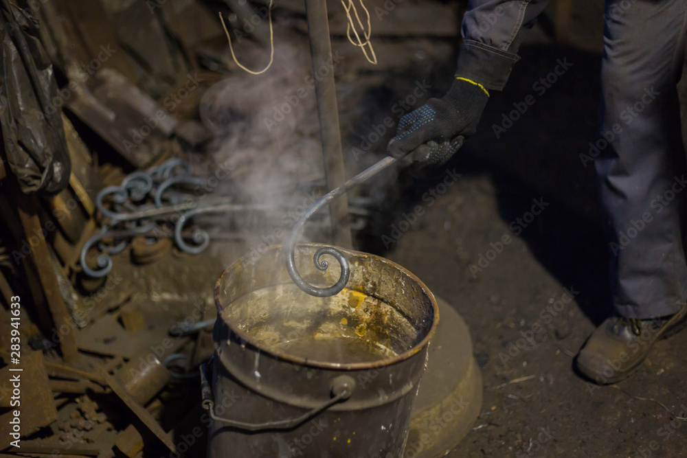 Professional blacksmith working with metal - quenching hot iron part in ...