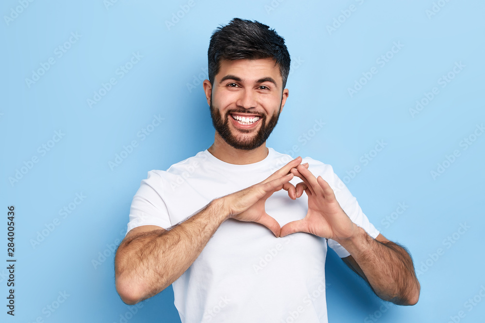 handsome cheerful guy is making a heart shape symbol with his fingers ...