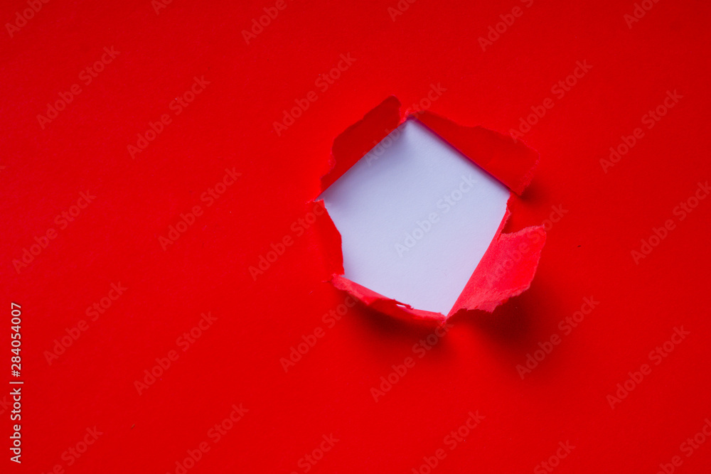 Torn red coloured paper on white background with closeup hole in the ...