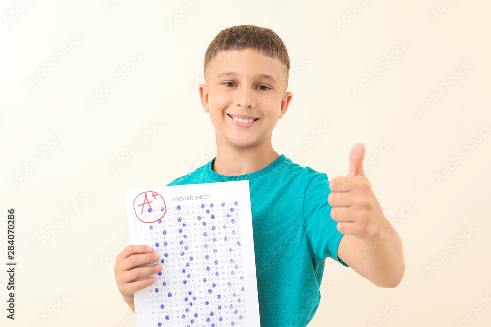 Happy boy with answer sheet for school test showing thumb-up on light ...