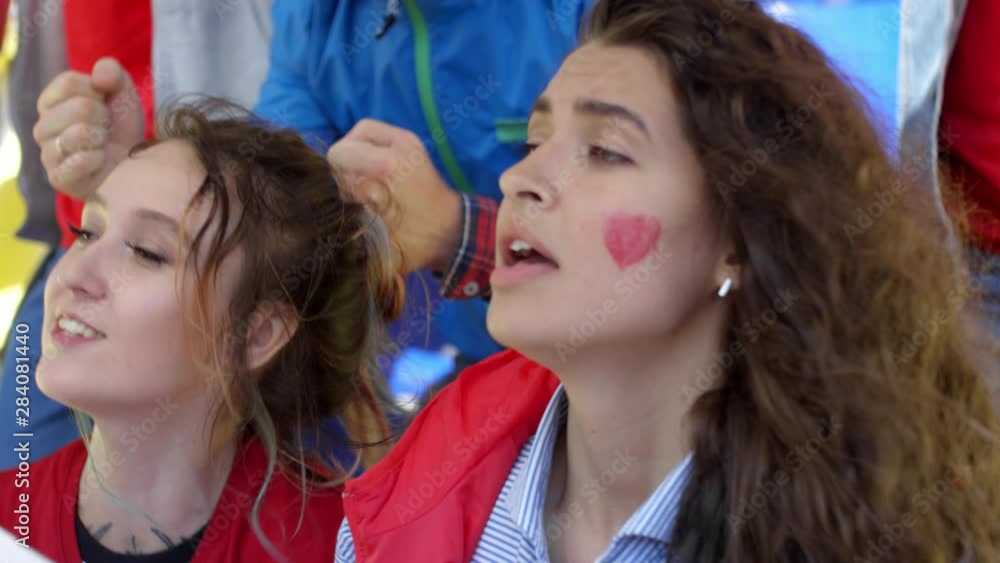Chest-up shot of two young female fans anxiously cheering on their team ...