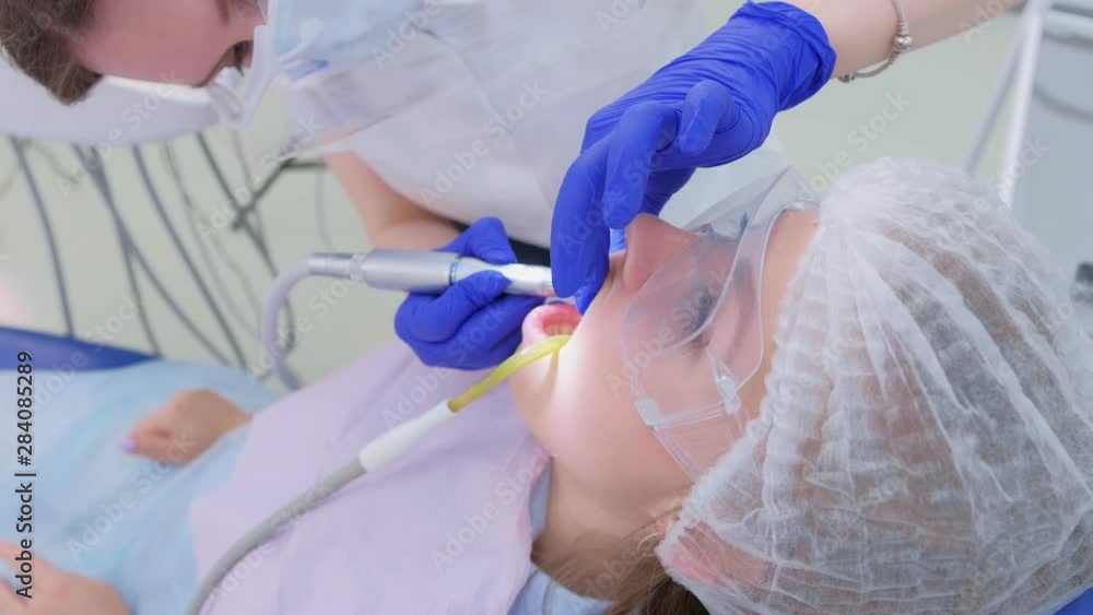 Dentist cleaning brushing and polishing woman's teeth uses drill in ...