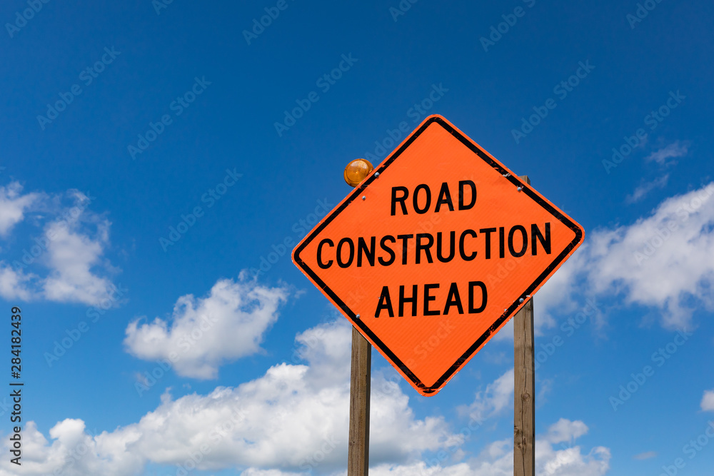 closeup of road construction ahead sign and warning light with blue sky ...