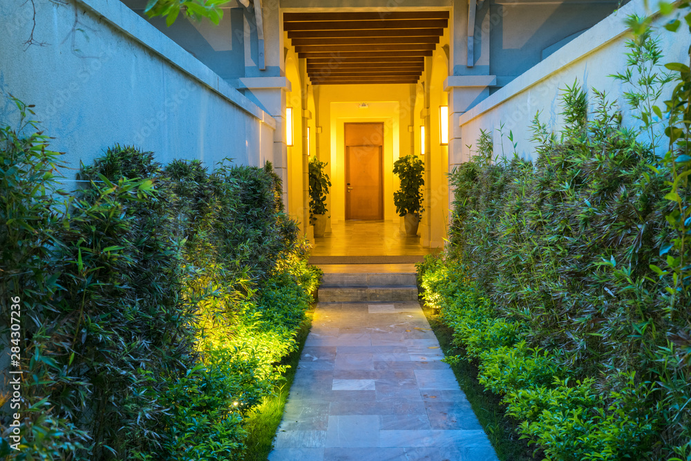 Garden path in resort with warm light and trees on side at evening ...