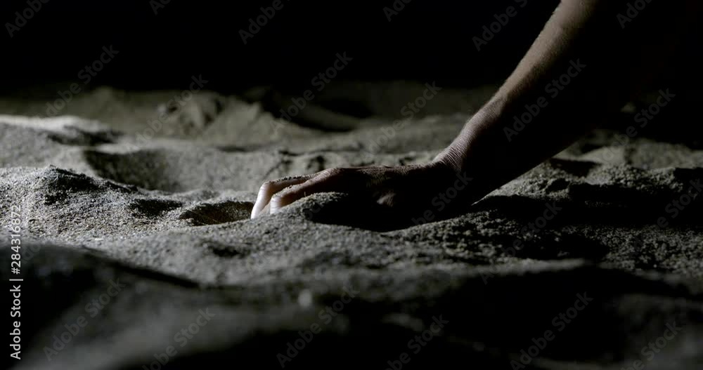 human hand in anger blow to the sand in the dark on the beach at night ...