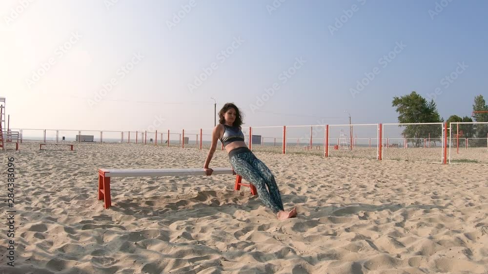 Athletic girl performs various gymnastic exercises on the bench and ...