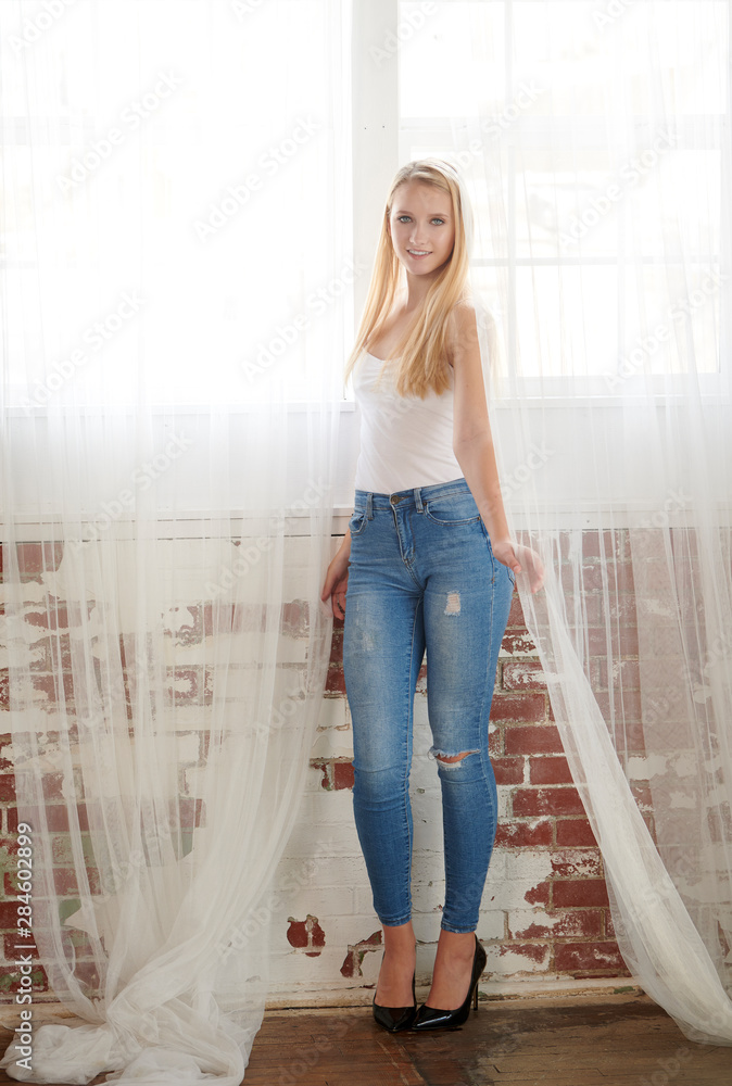 Beautiful blonde young woman (model) poses in studio wearing white tank ...