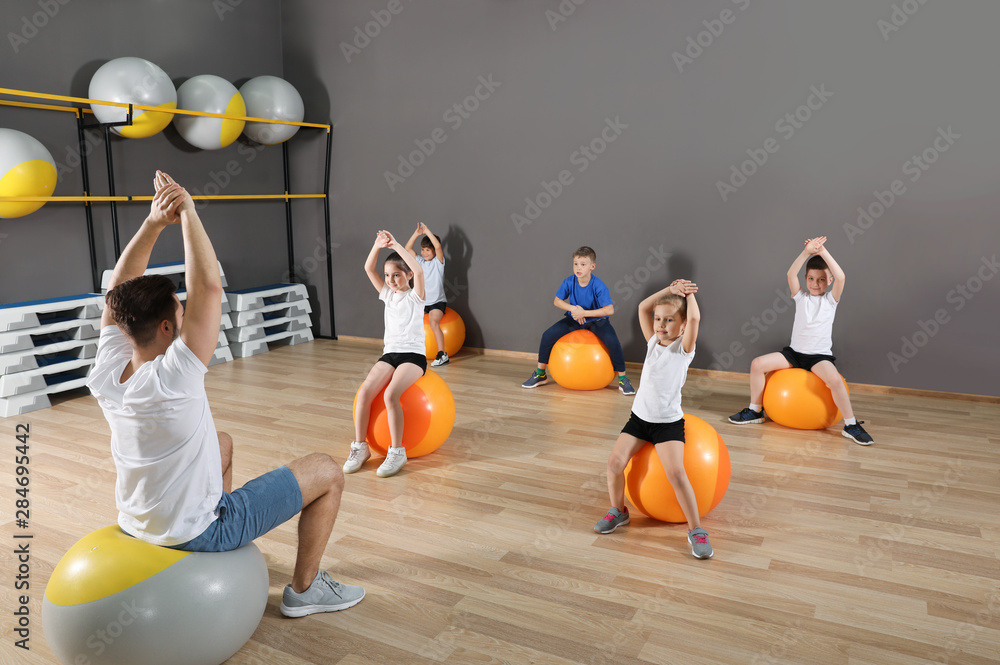 Cute little children and trainer doing physical exercise in school gym ...