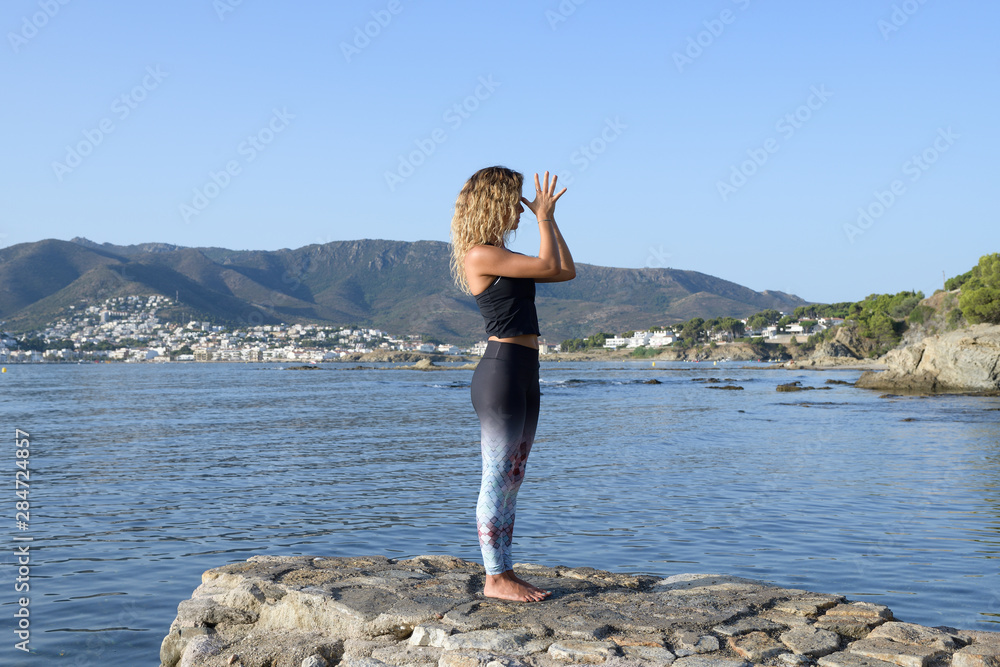 Young girl doing yoga on a small beach pier with a Mediterranean ...
