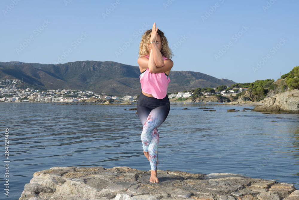 Young girl doing yoga on a small beach pier with a Mediterranean ...