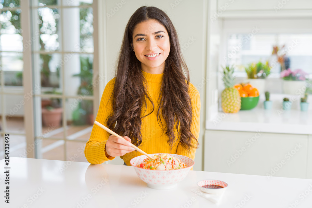 Young woman eating a bowl of Asian rice using chopsticks with a happy ...