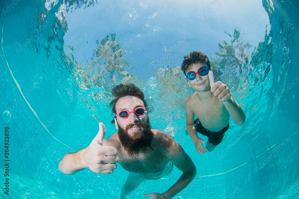 Father and son diving and swimming under water in pool during summer ...