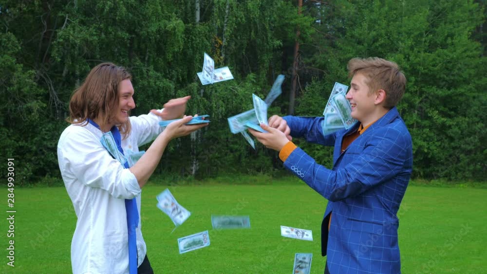 Two young man throw money (100 dollar bill) into the air in a park in ...