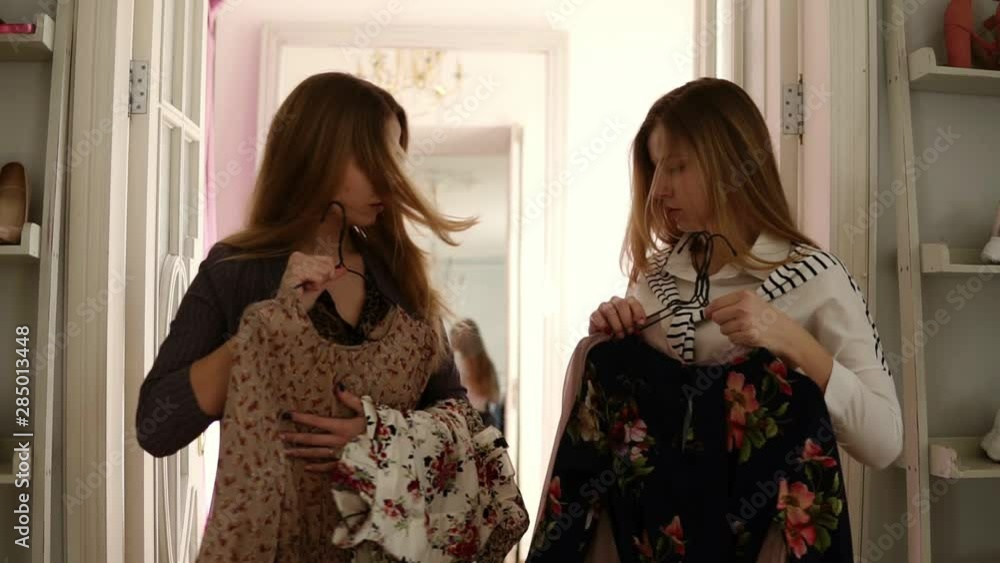 Two beautiful females, twin sisters holding hangers with clothes in ...