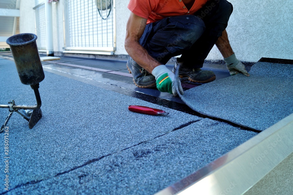 worker installing tar foil on the rooftop of building. Flat roof ...