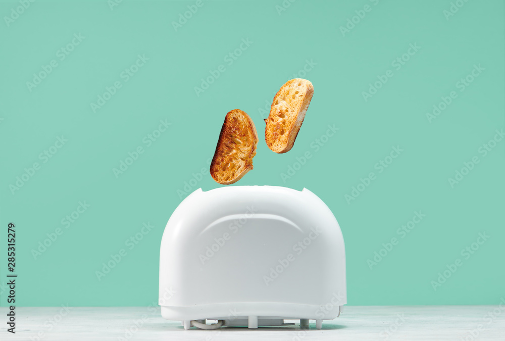 Roasted toast bread popping up of toaster with green wall, front view ...