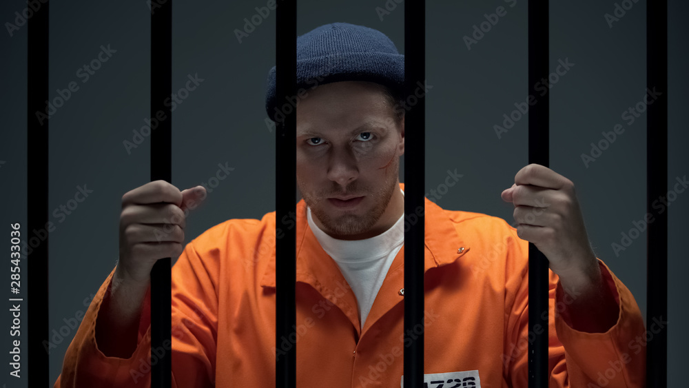 Angry Caucasian prisoner with scared face looking through cell bars ...
