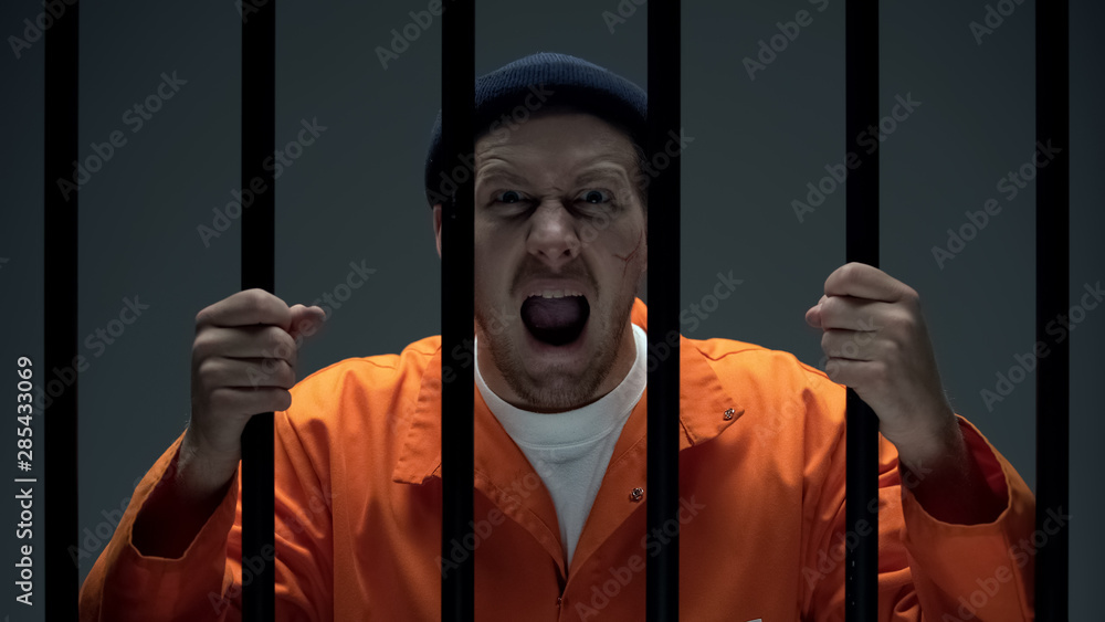 Aggressive dangerous male prisoner with scar on face holding bars and ...