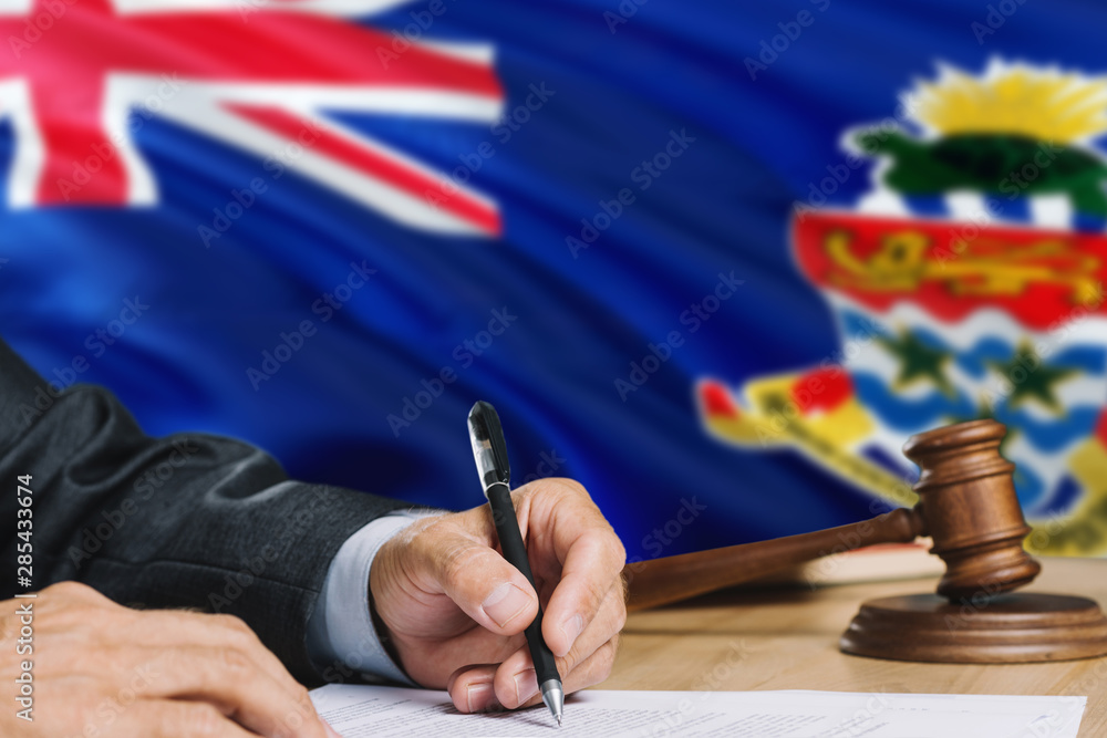 Judge writing on paper in courtroom with Cayman Islands flag background ...