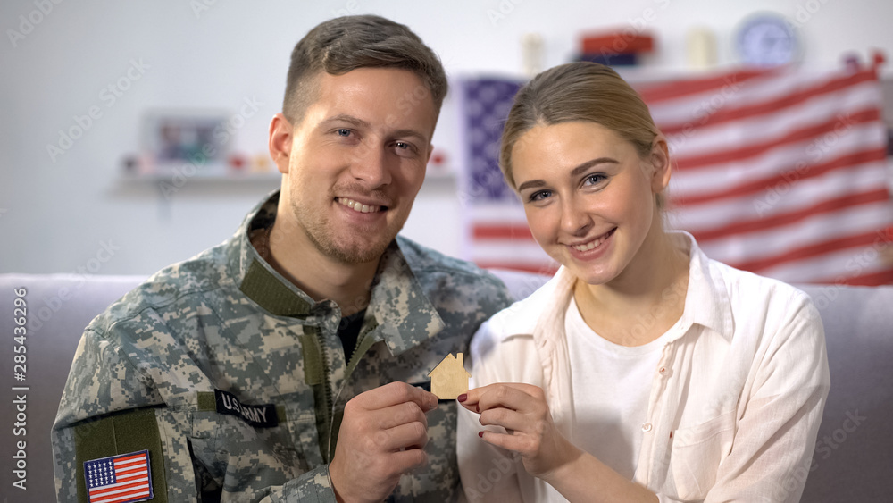 Smiling US male soldier and his wife showing wooden house sign on ...