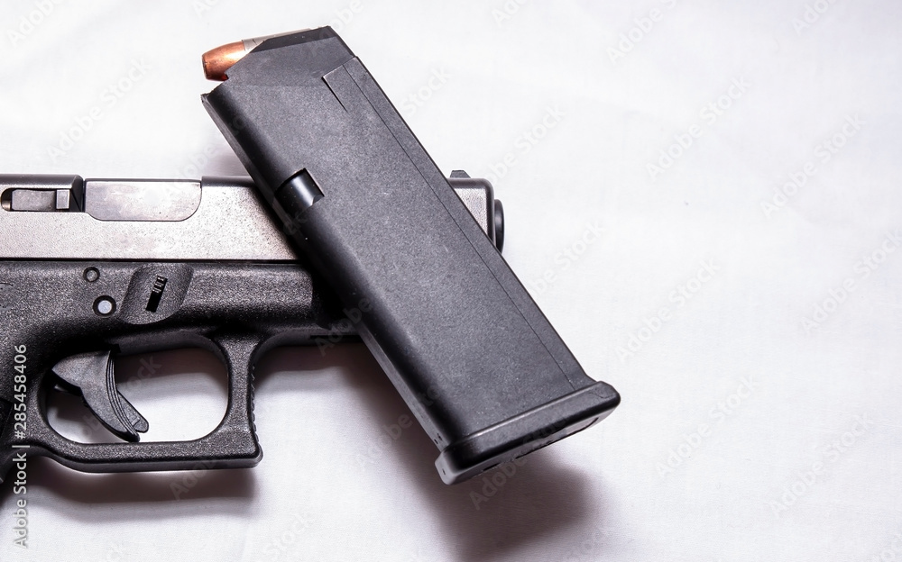 A loaded 9mm pistol magazine on top of a black 9mm pistol on a white ...