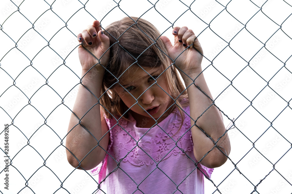 Sad girl behind metal wire mesh fence. Abandoned upset and lonely child ...