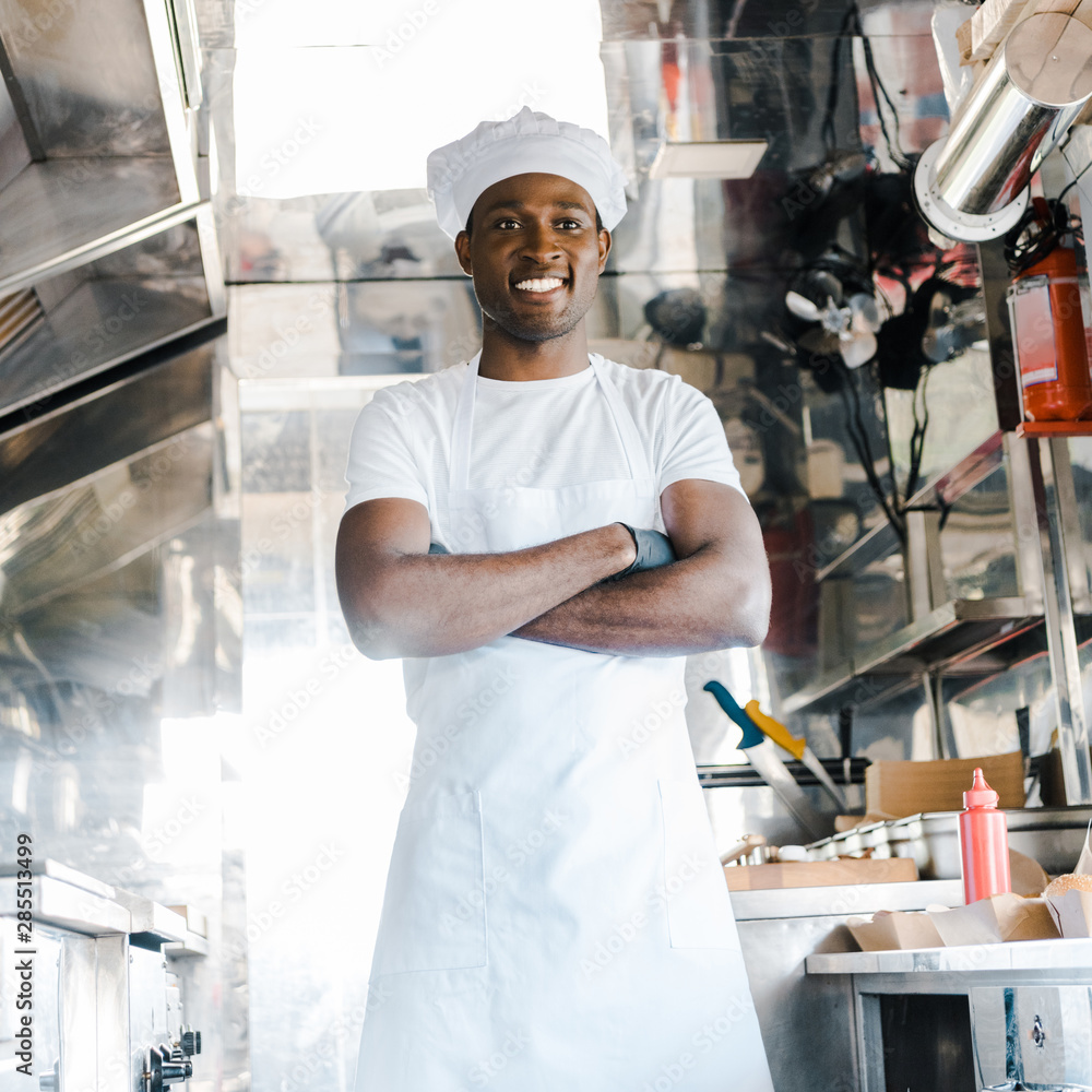 positive african american chef standing with crossed arms in food truck ...