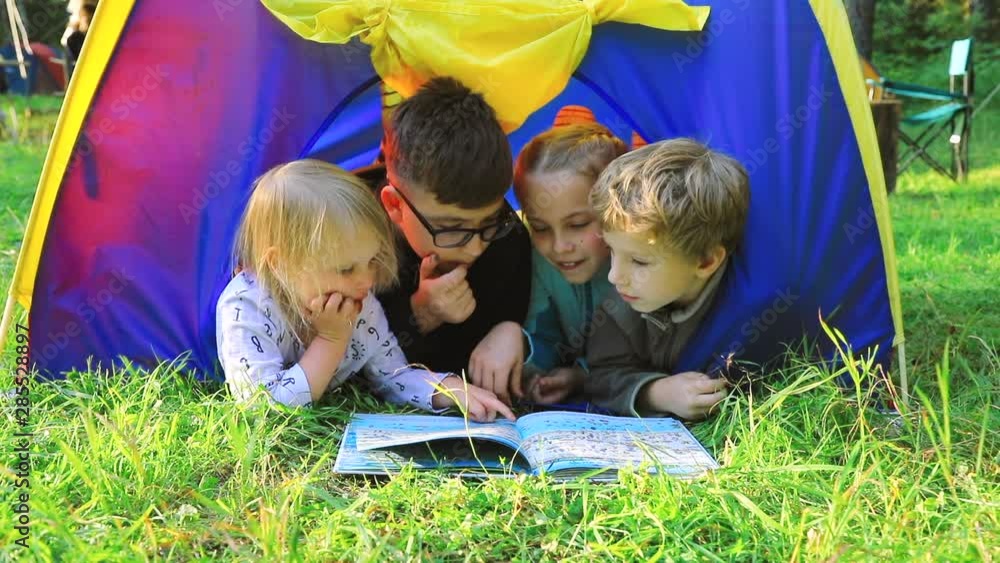 Four children of different age reading a book while lying together in ...