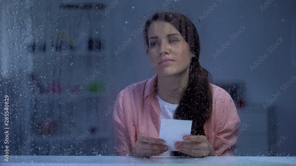 Sad woman with photo feeling sad behind rainy window, remembering first ...