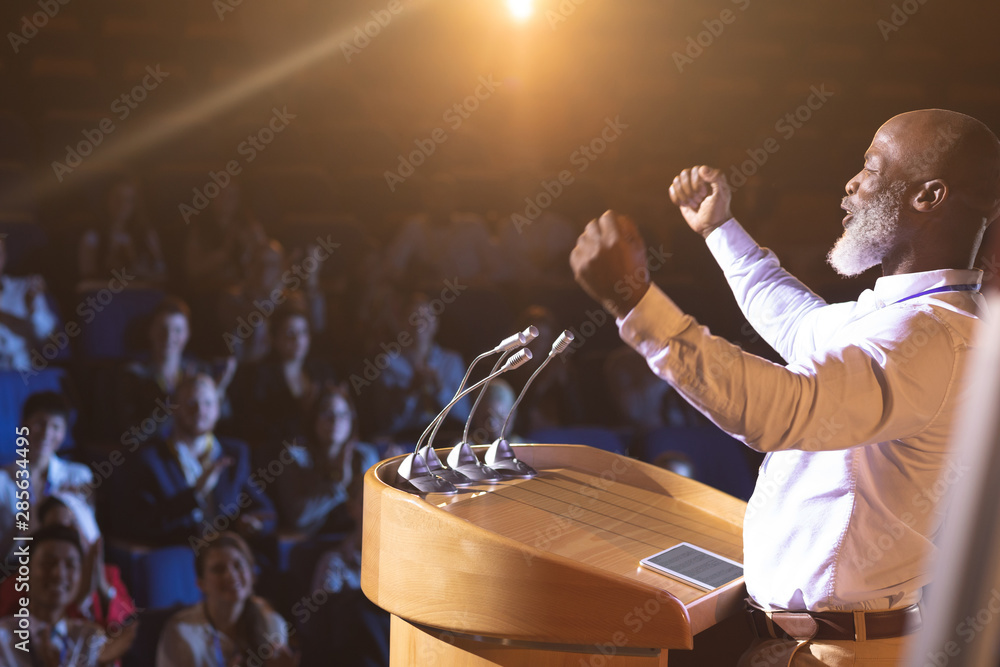 Businessman standing near podium and giving speech to the audience in ...