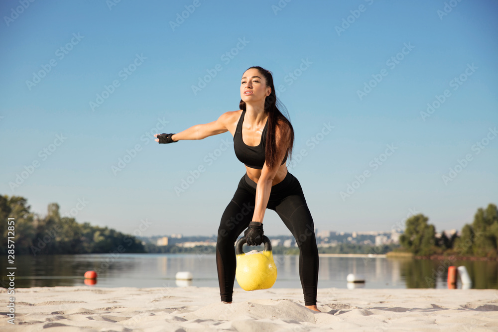 Young healthy woman training upper body with weights at the beach ...