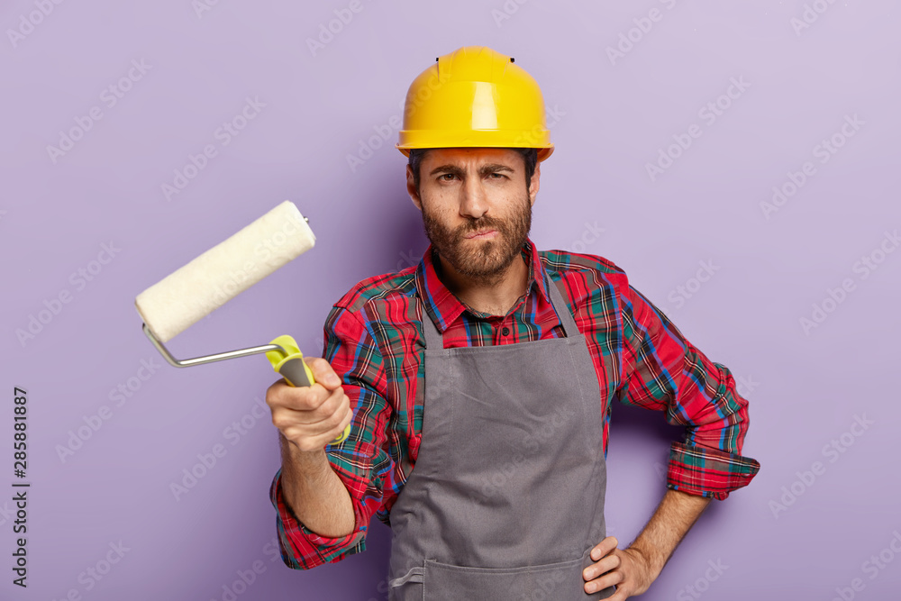 Serious man painter holds painting roller, does redecoration at home ...