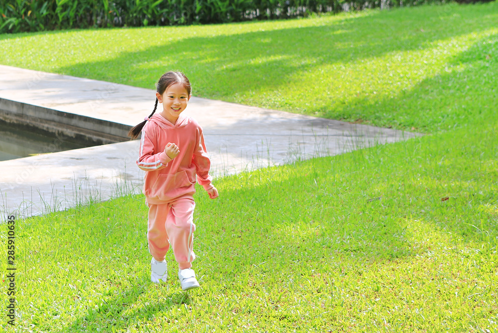 Smiling little Asian child girl in pink tracksuit running in the green ...