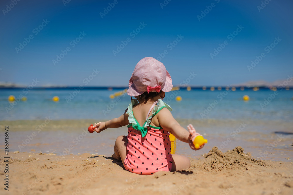 back view photo of a little girl in swimsuit and pink hat sitting on ...