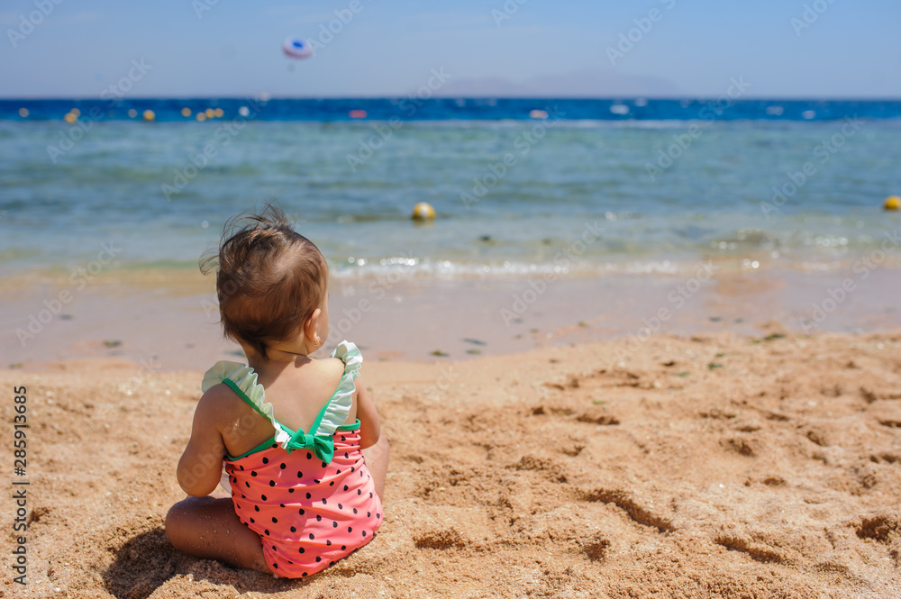 back view photo of a little girl in swimsuit and pink hat sitting on ...